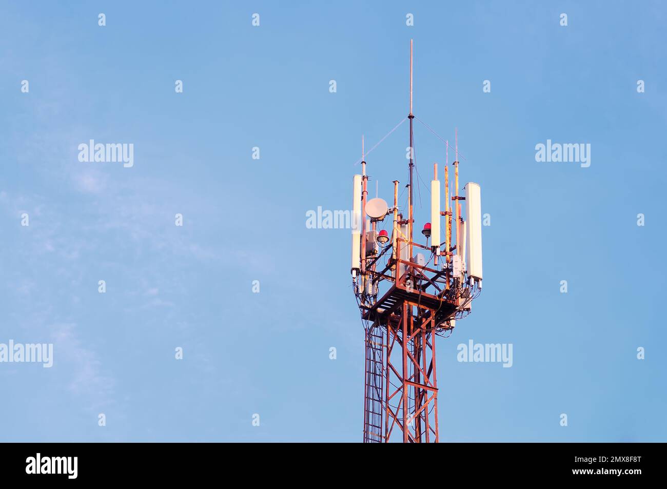 High antenna of mobile communication on the background of the blue sky. Red steel tower frame ...