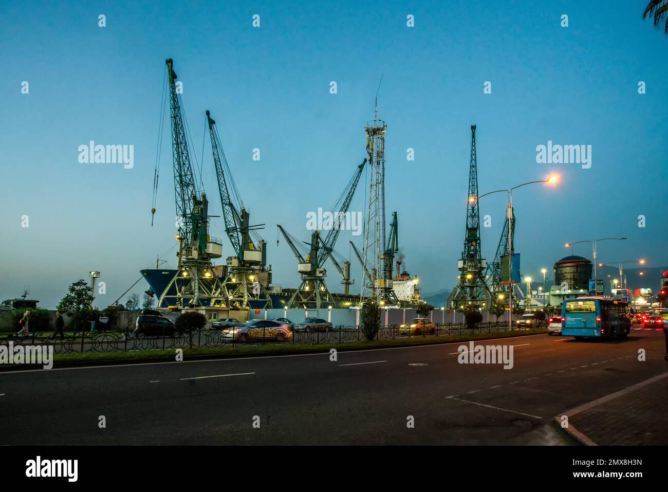Large port cranes in the port of Batumi at blue hour. Bus and cars on ...