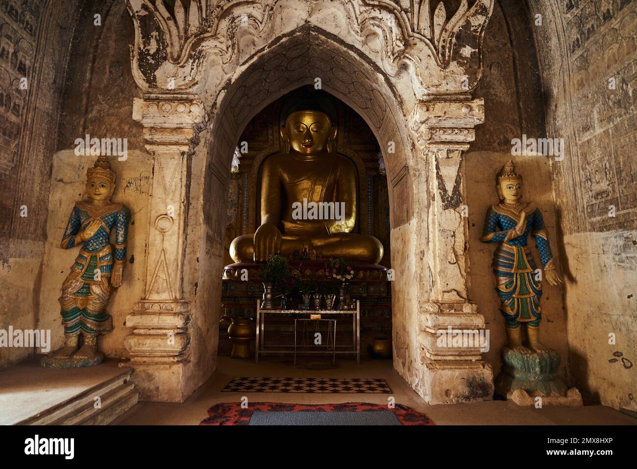 A large golden Buddha statue sitting in an ancient temple in Bagan ...