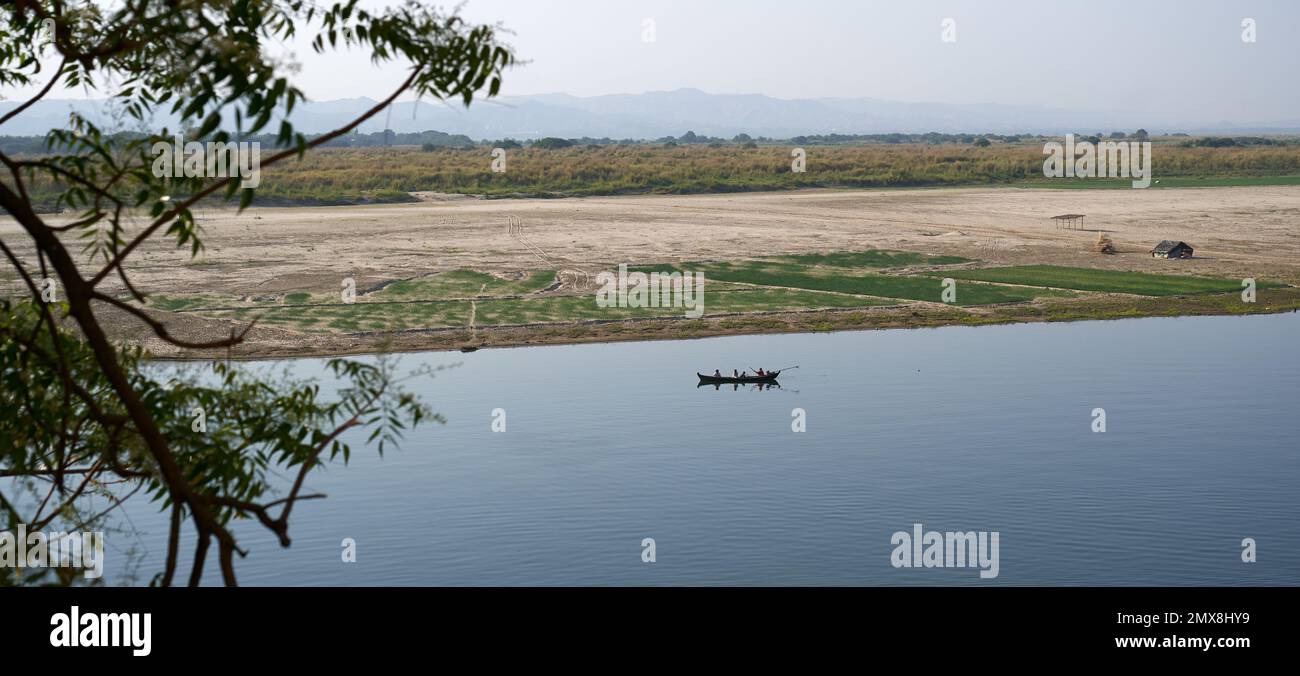 A single fishing boat travels down the Irrawaddy River in the midday ...