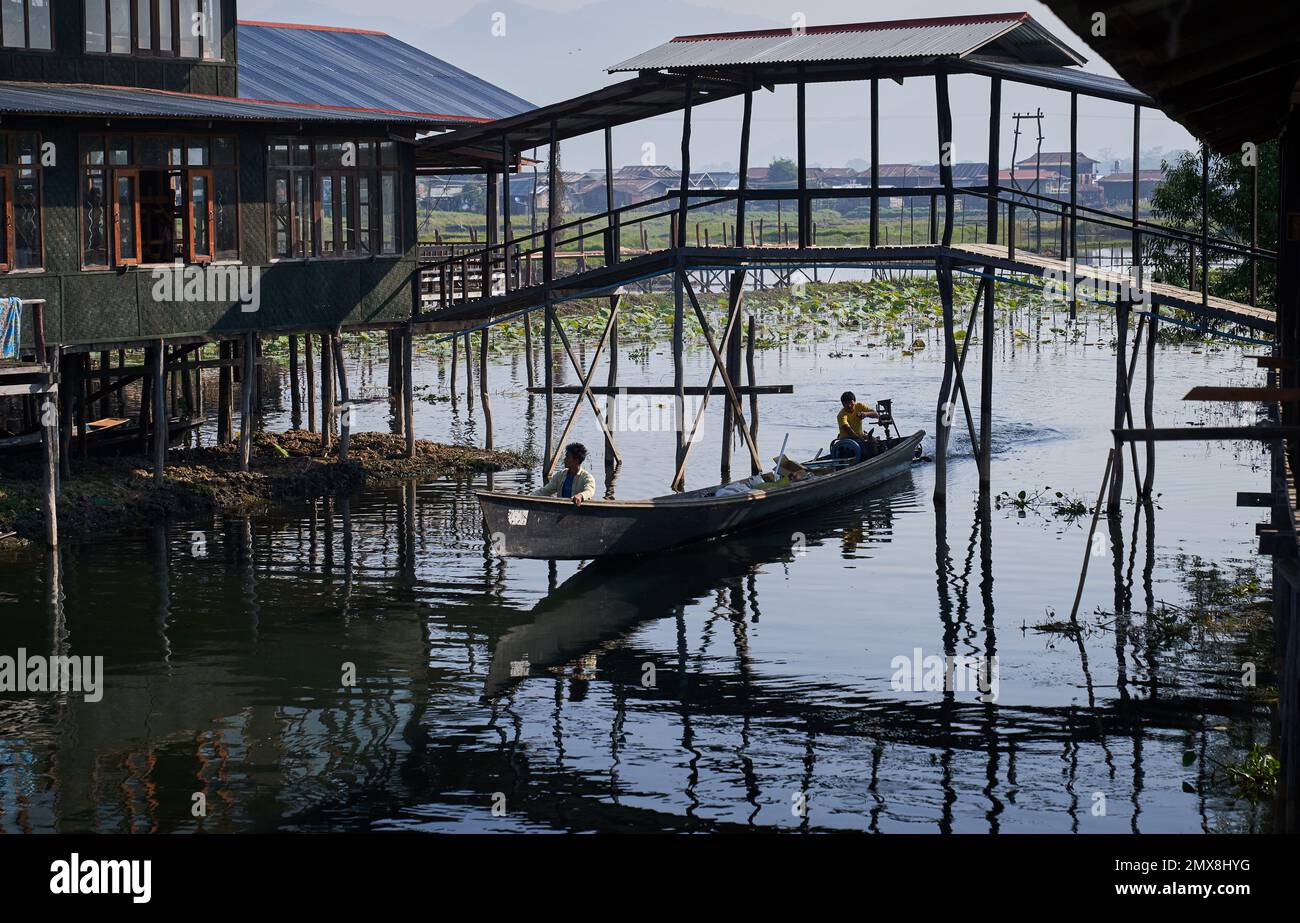 A wooden longboat passes under a traditional stilt bridge in a floating ...