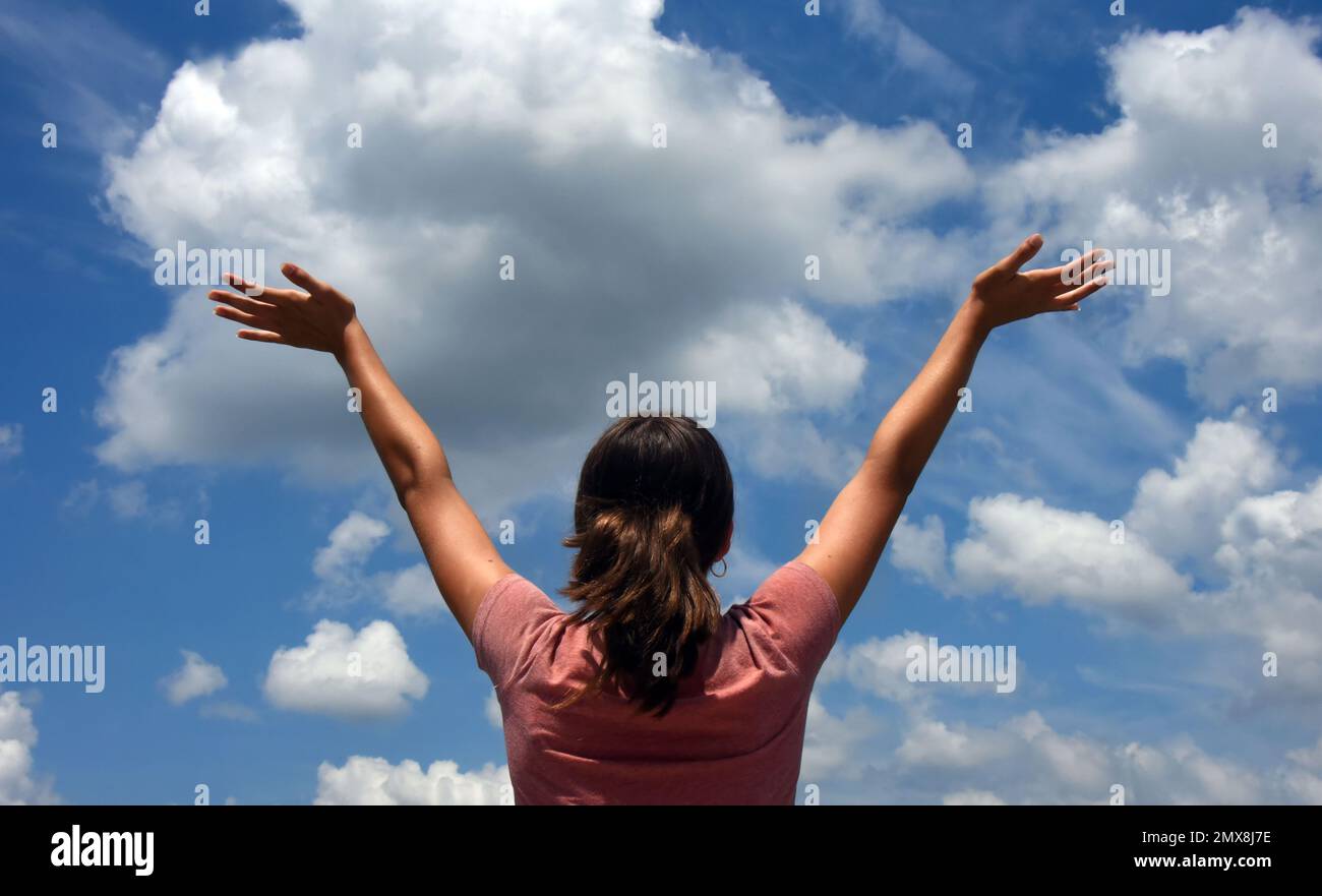 Young teenage girl stands, looking upward, with arms outstretched ...