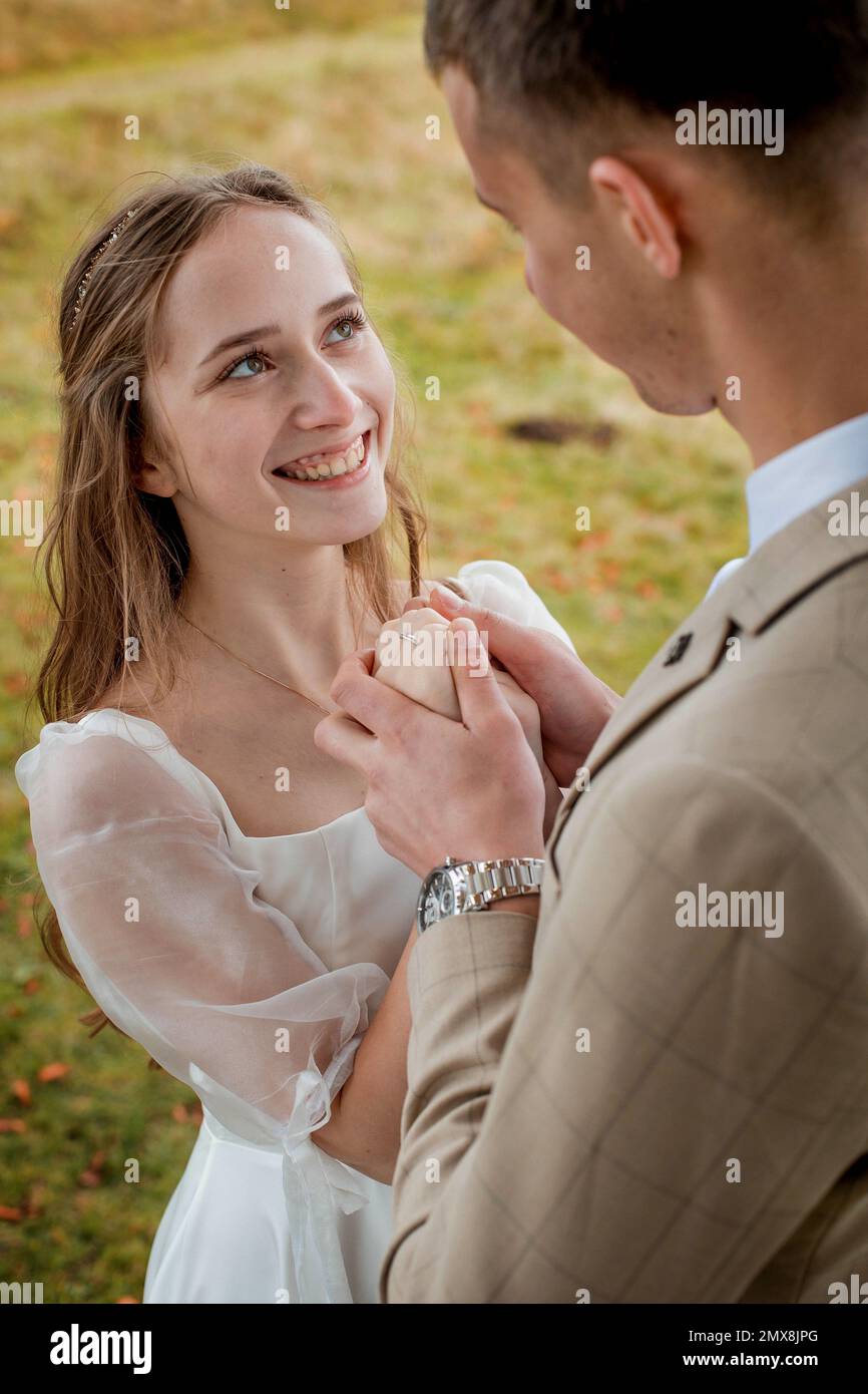 The bride looks at the groom with loving eyes. Smiling newlyweds look ...