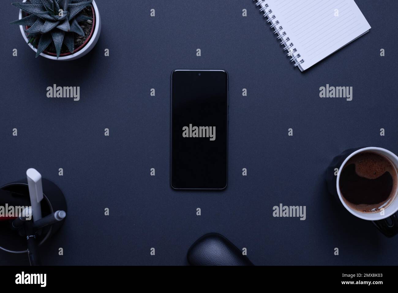 Blank mobile phone on black desk surrounded by office supplies ...