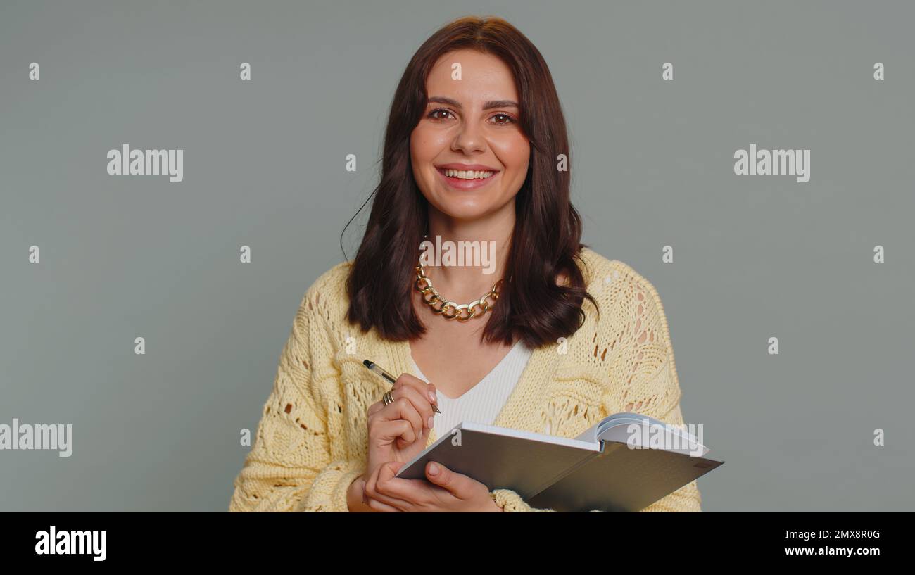Thoughtful journalist pretty young woman in cardigan making notes ...