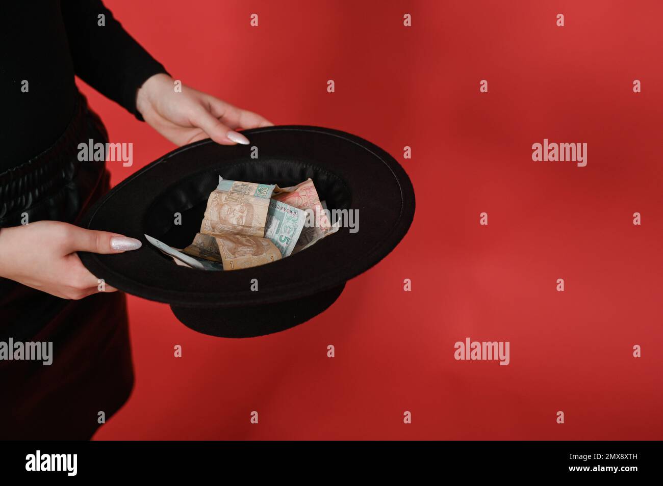 a hat with money. ask for money. black hat in hand. on a red background ...