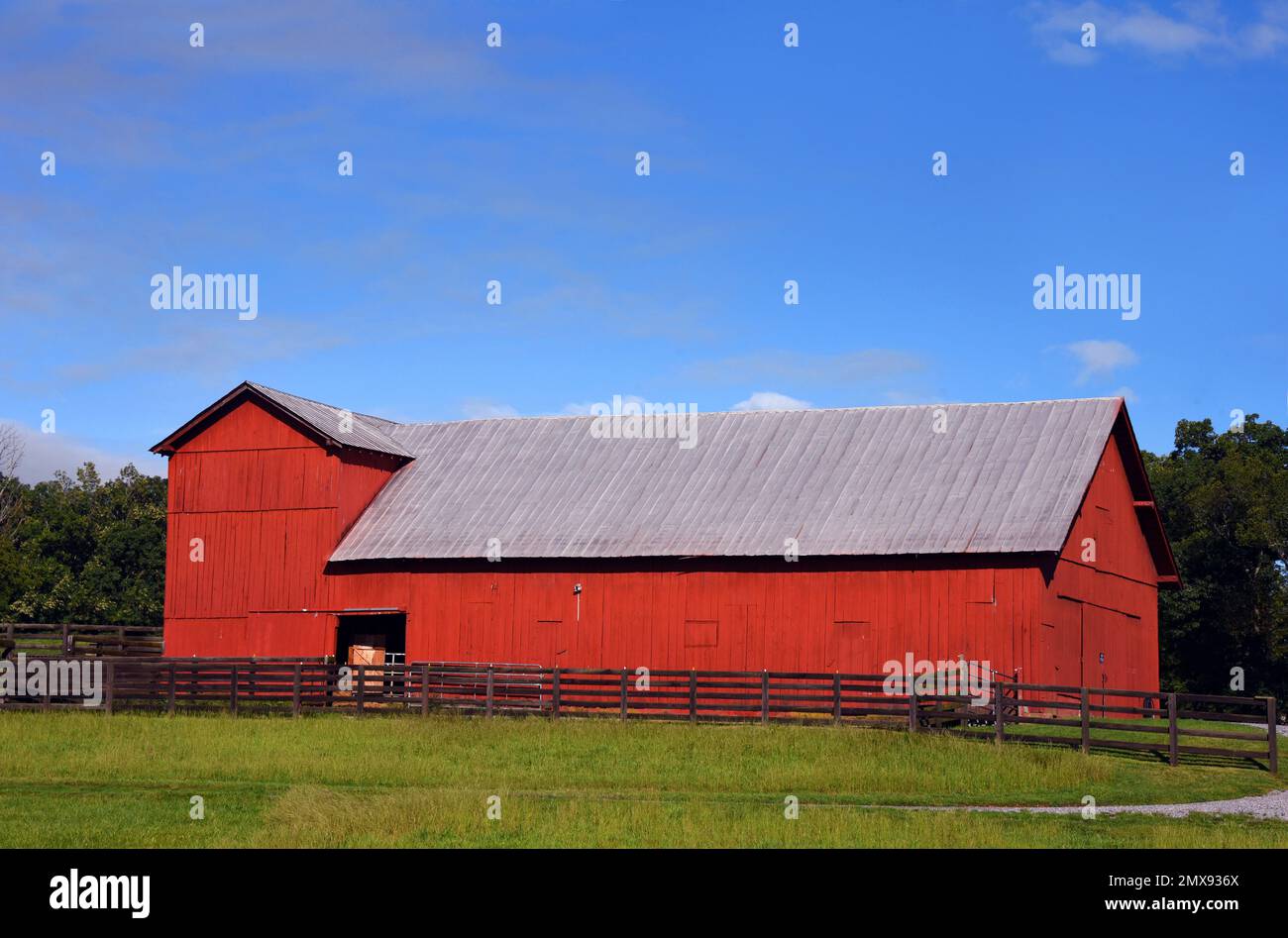 Red, wooden, barn is large and has a tin roof. Rustic fence surrounds ...