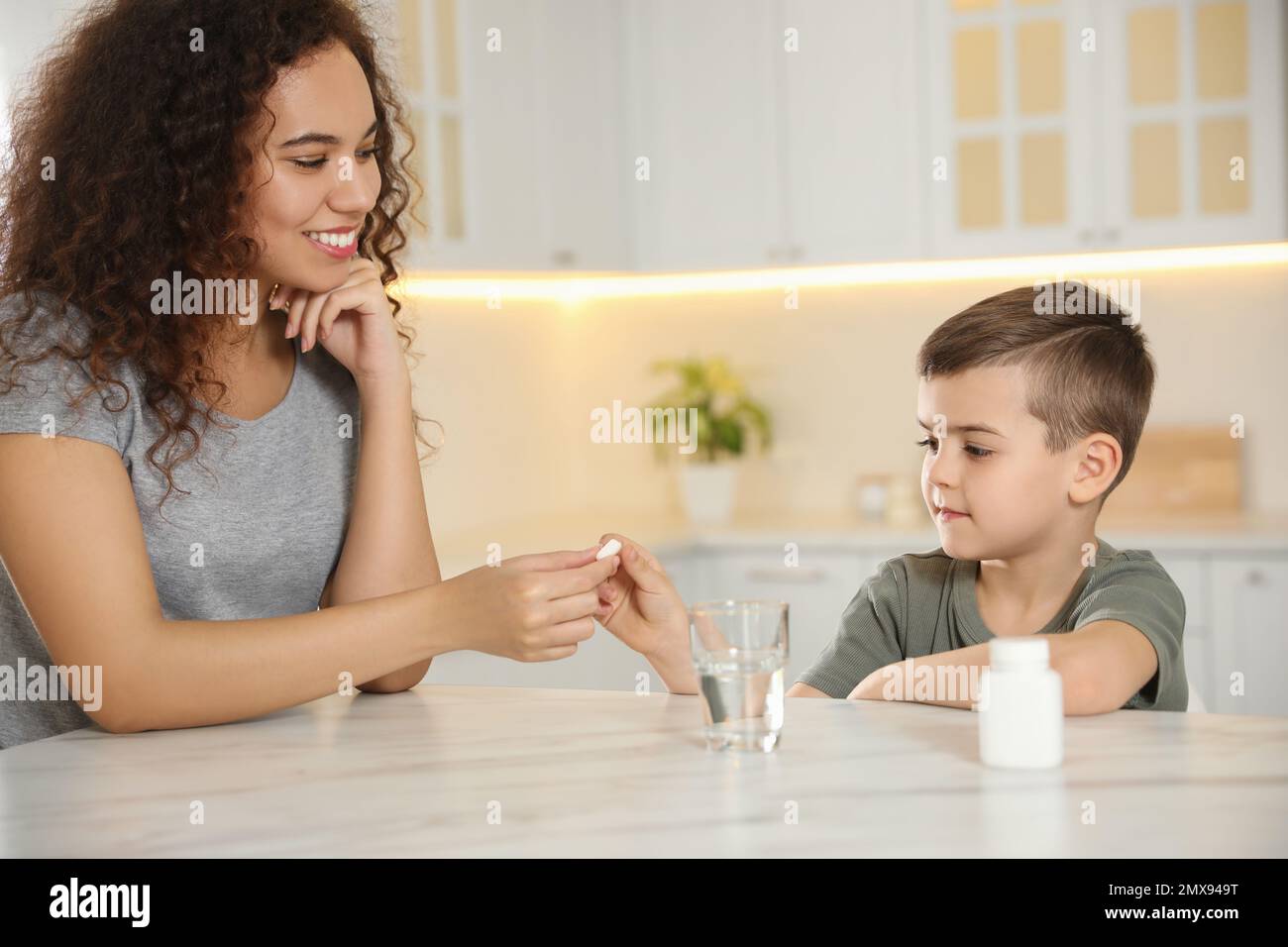 African-American woman giving vitamin pill to little boy in kitchen ...
