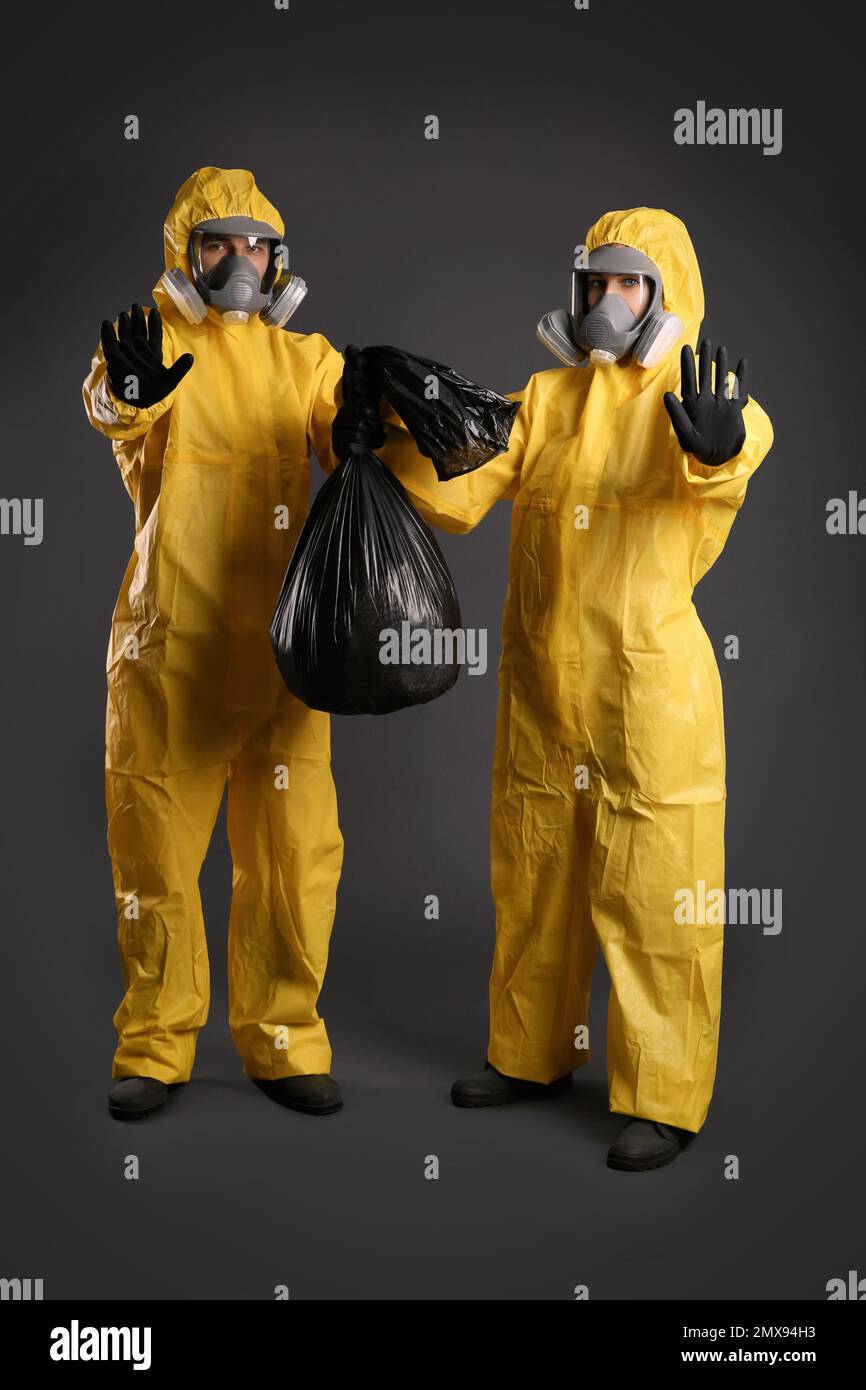 Man and woman wearing chemical protective suits holding trash bag on ...