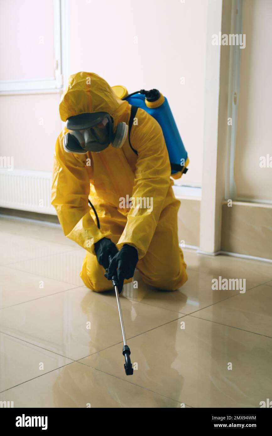 Pest control worker in protective suit spraying pesticide indoors Stock ...