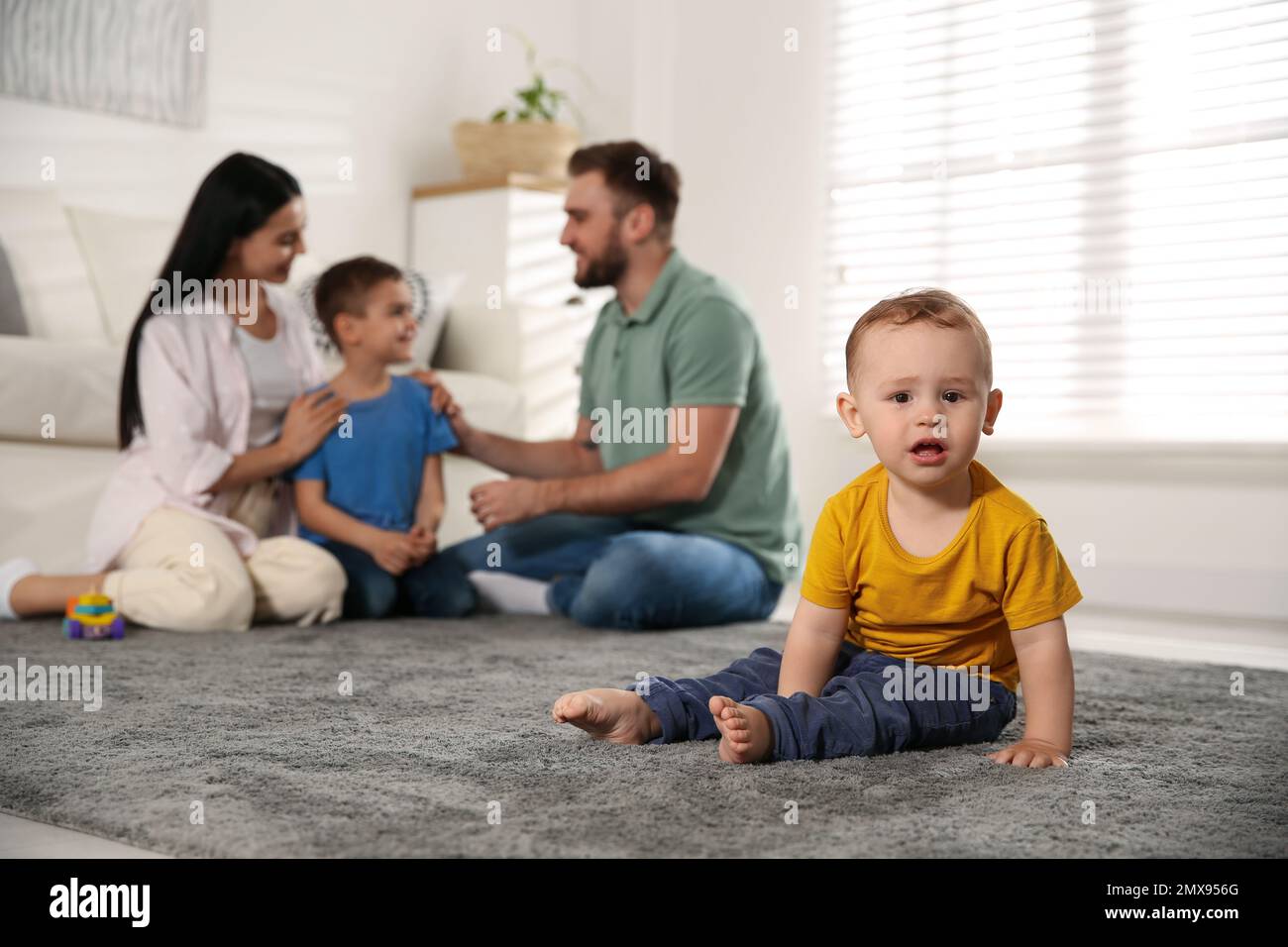 Unhappy baby sitting alone on floor while parents spending time with ...