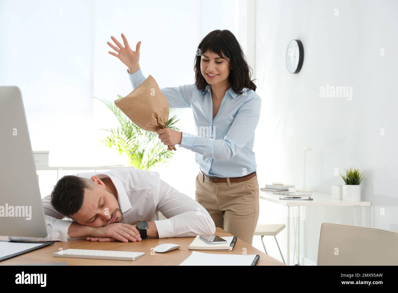 Young woman popping paper bag behind her sleeping colleague in office ...