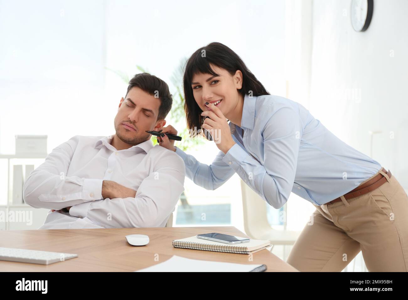 Young woman drawing on colleague's face while he sleeping at workplace ...