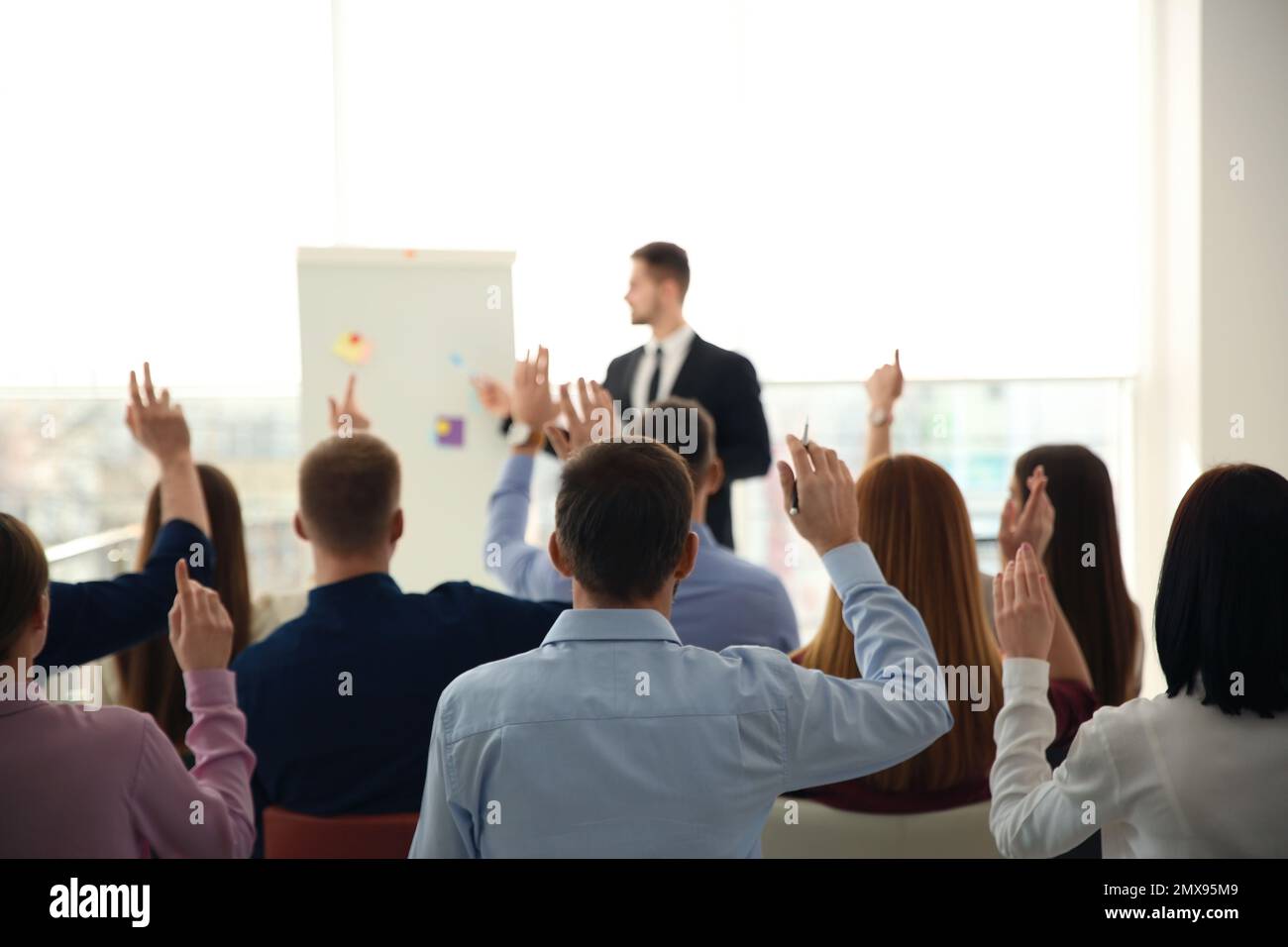 People raising hands to ask questions at business training indoors ...