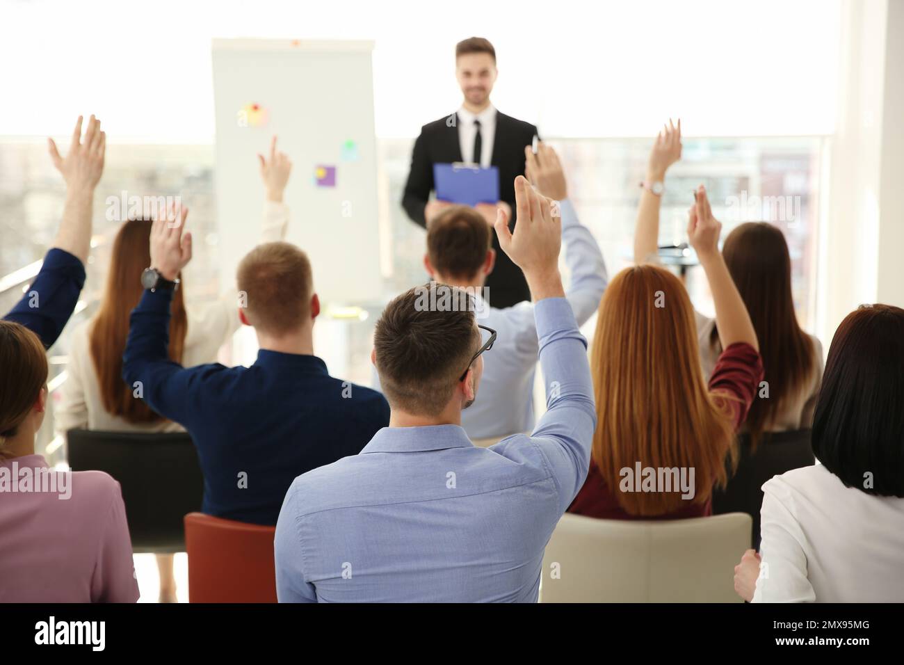 People raising hands to ask questions at business training indoors ...
