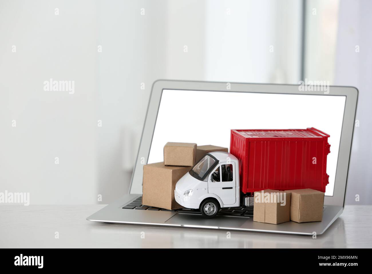 Laptop and truck model with boxes on table indoors. Courier service ...