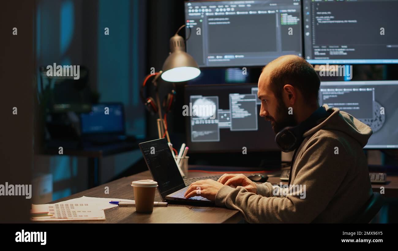 Young male developer typing server code on multiple screens using coding language on laptop late ...