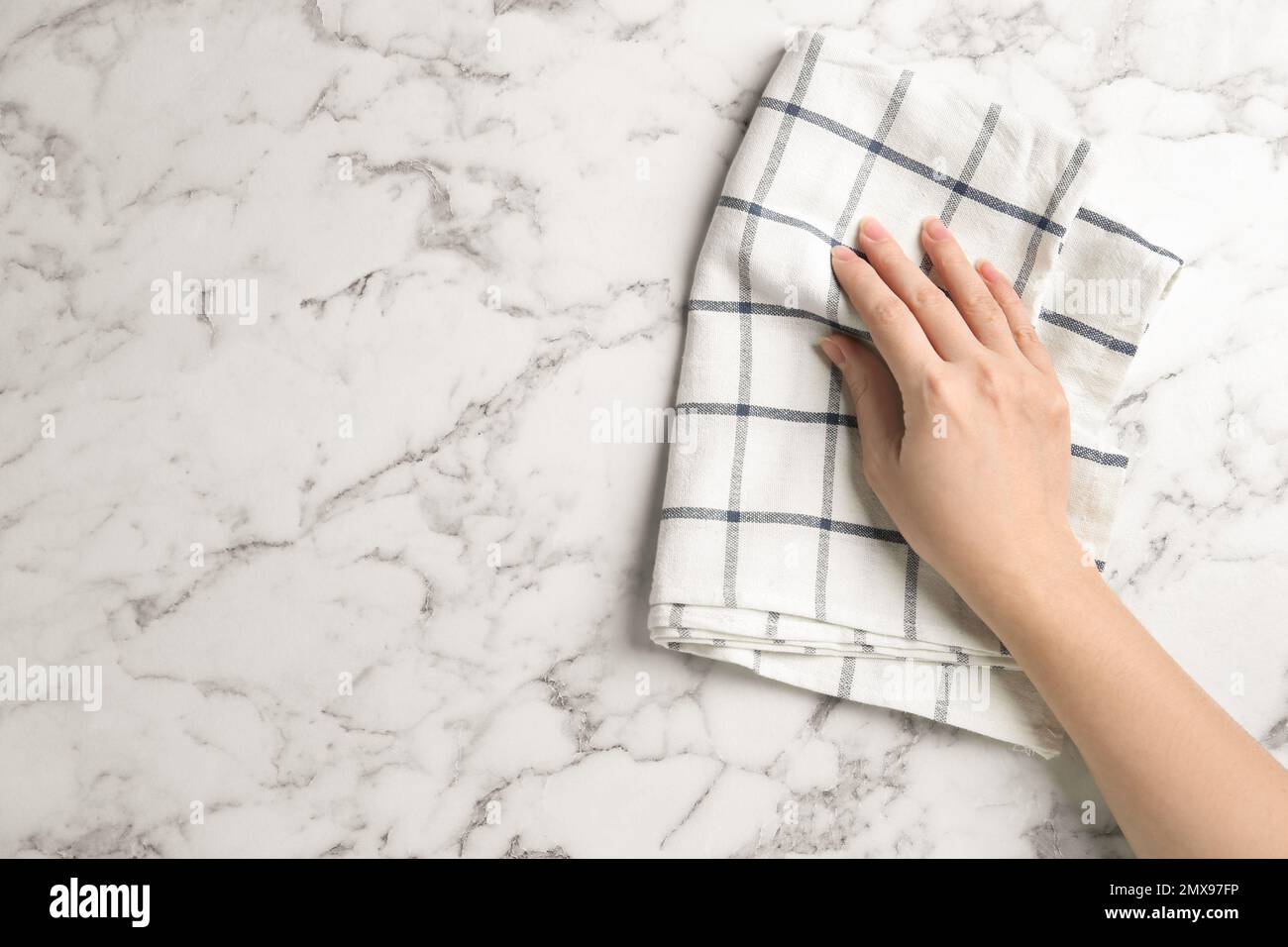 Woman wiping white marble table with kitchen towel, top view. Space for ...