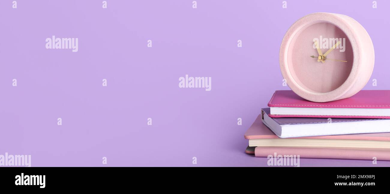 Alarm clock with notebooks on lilac background with space for text ...