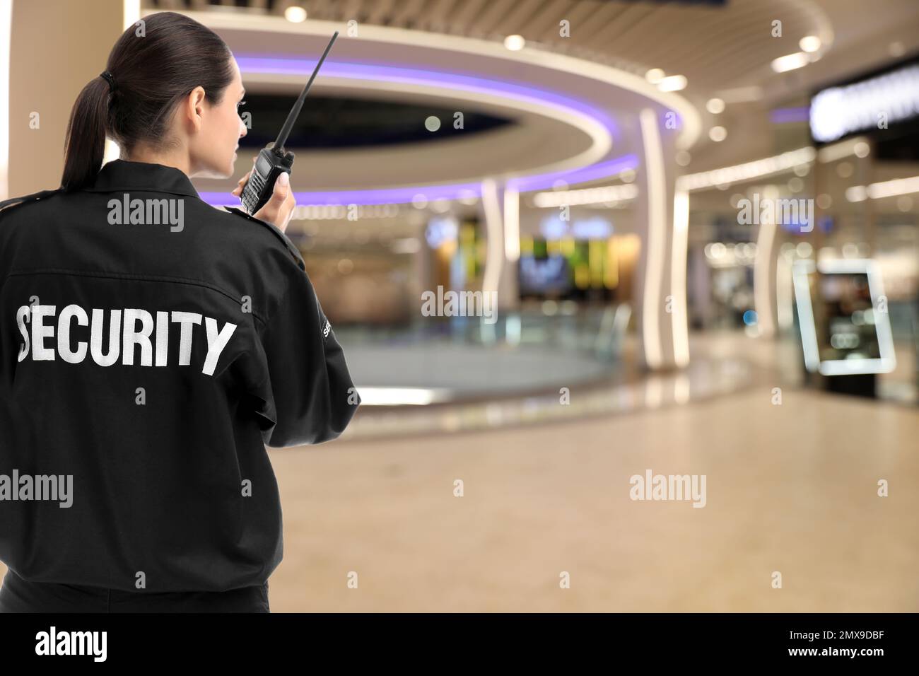 Security guard using portable radio transmitter in shopping mall, space ...