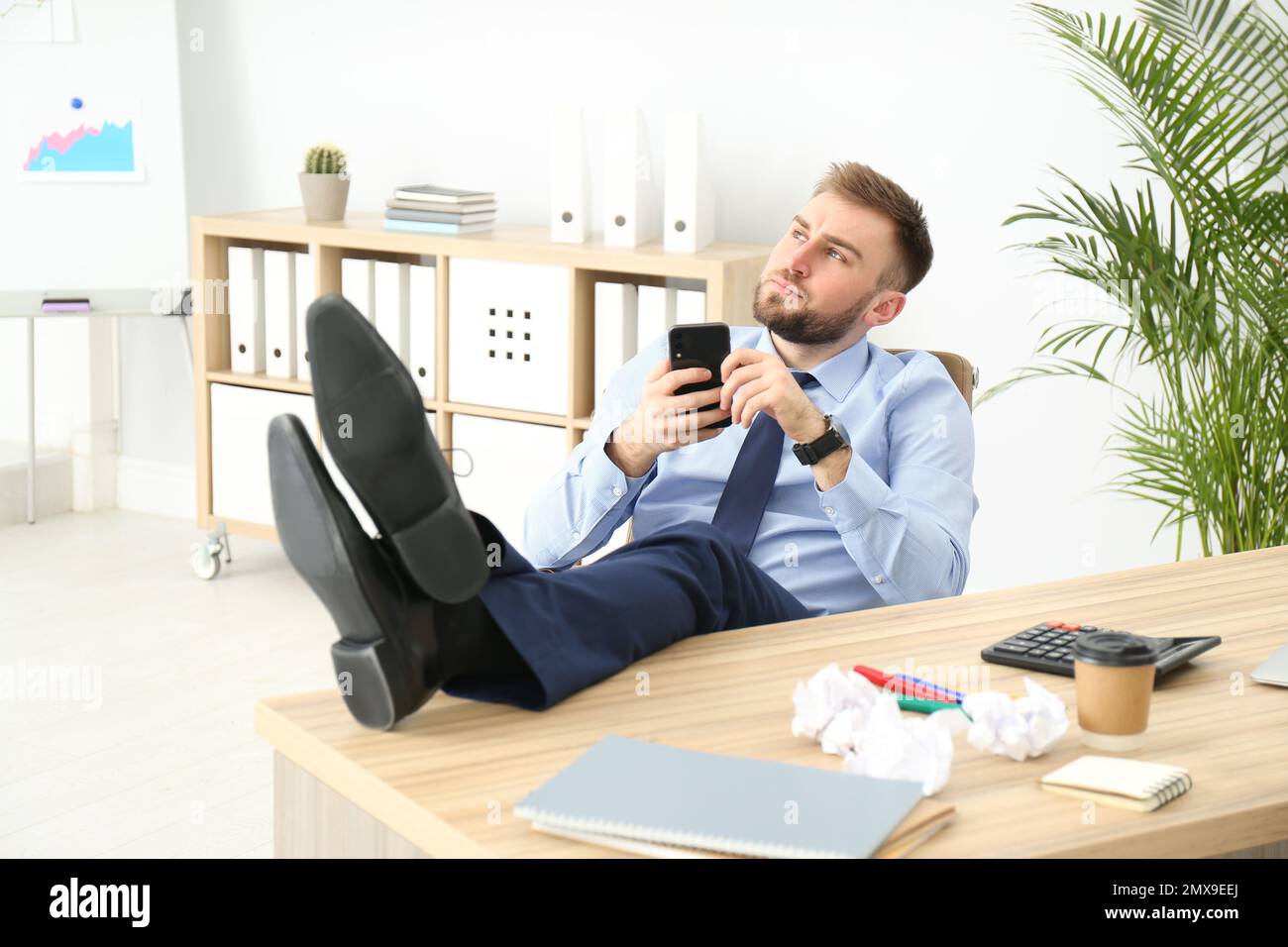 Lazy office employee with mobile phone at workplace Stock Photo - Alamy
