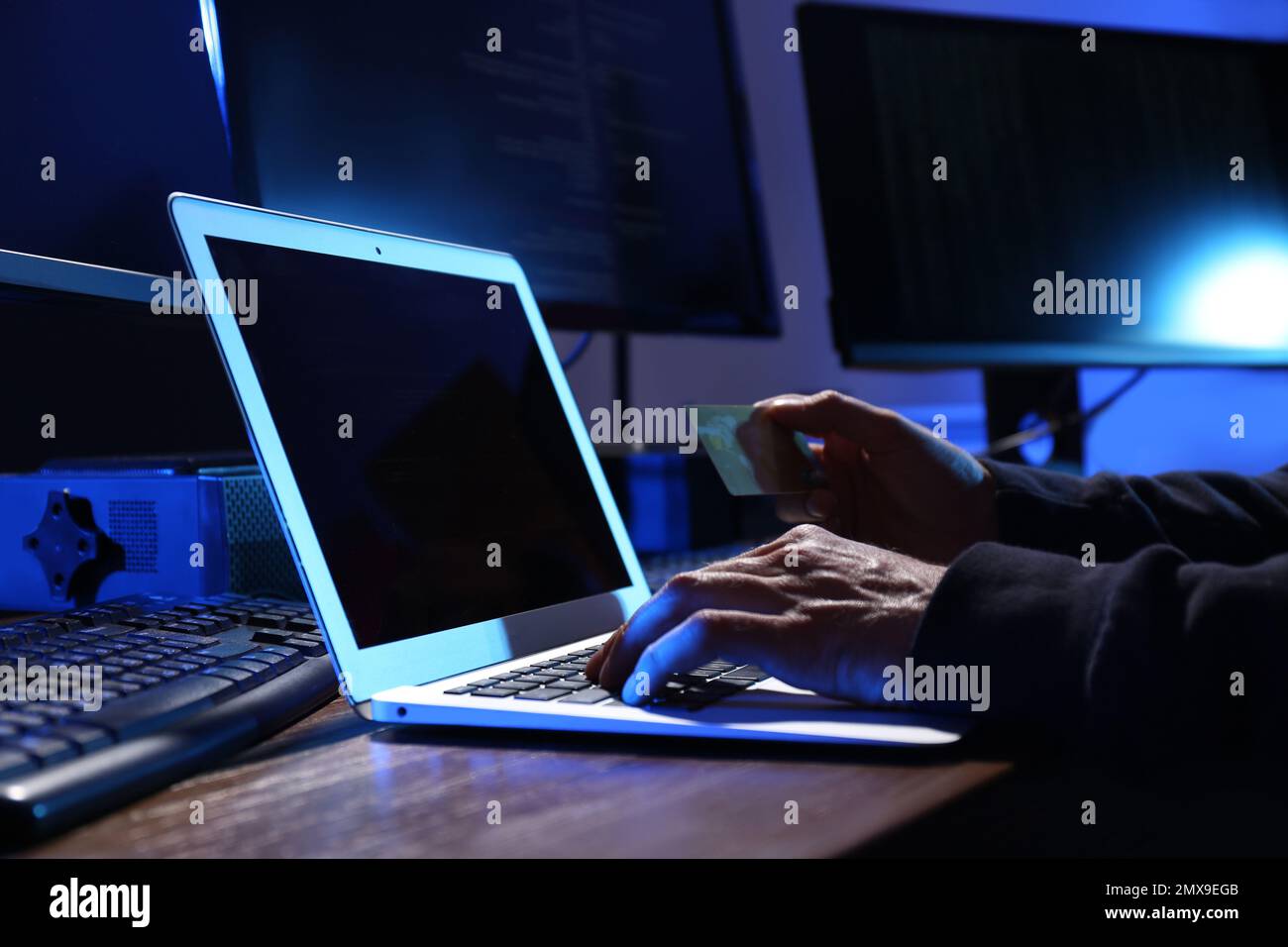 Hacker with computers and credit card in dark room, closeup. Cyber ...