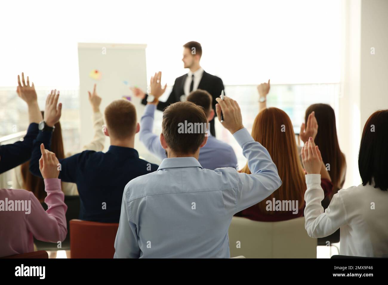 People raising hands to ask questions at business training indoors ...