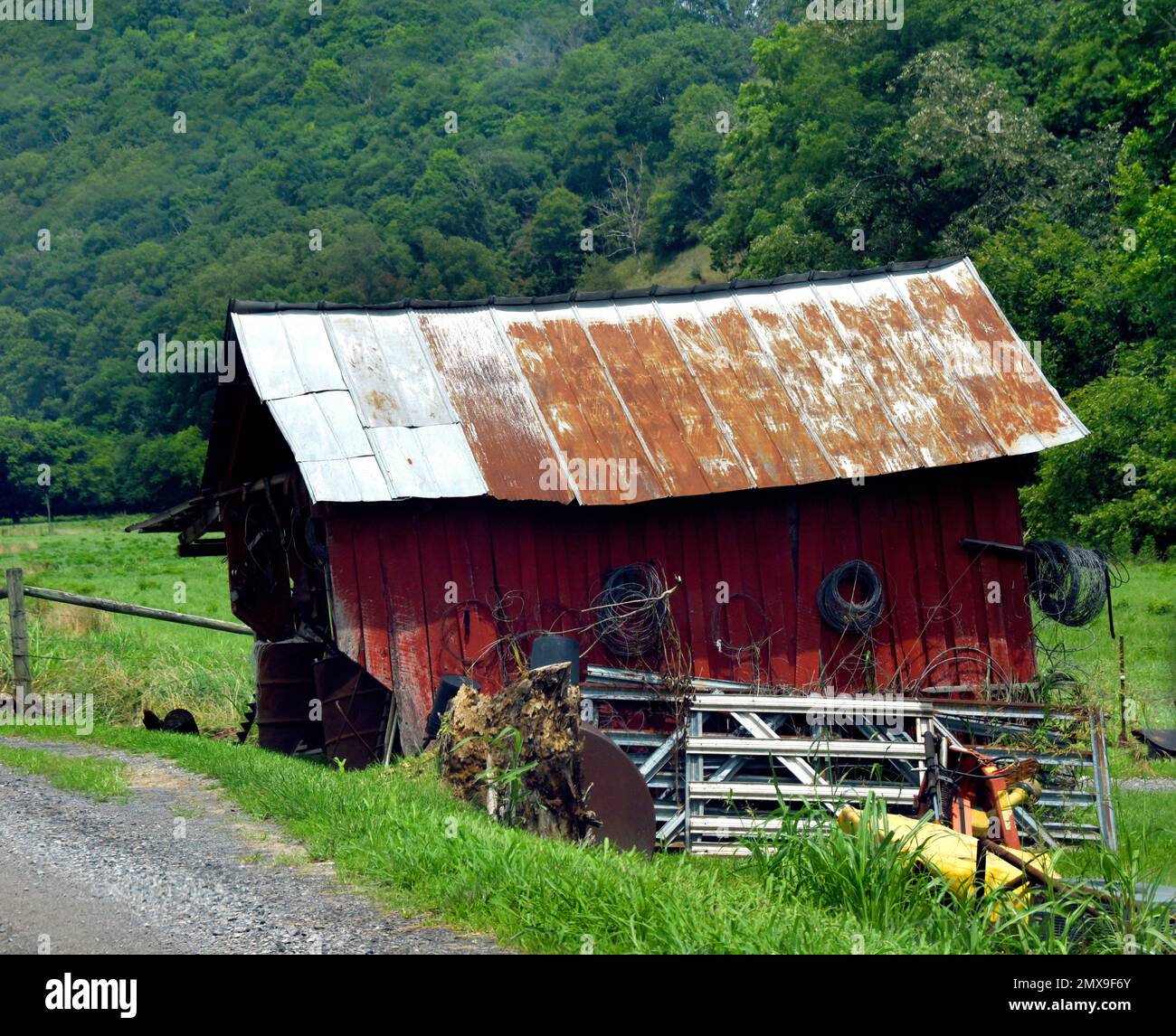 Farming equipment lays in disarray against a rustic, red, wooden barn ...