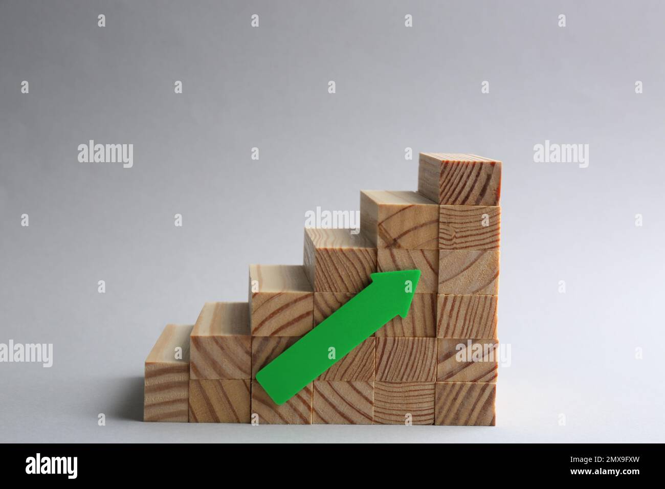 Stairs made of wooden blocks with green arrow on light grey background ...