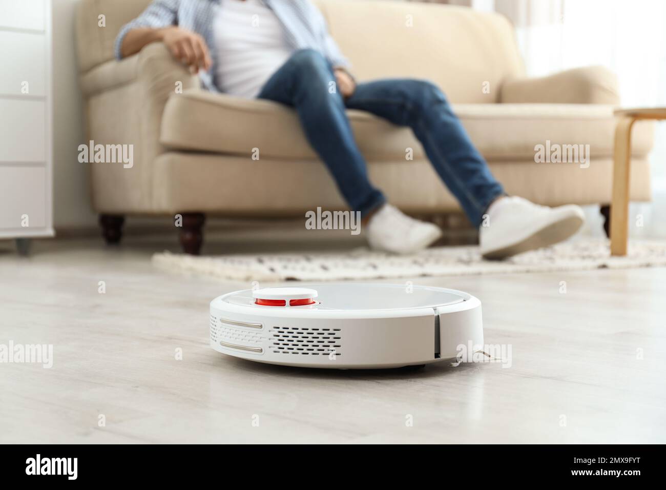 Man resting on sofa while robotic vacuum cleaner doing his work at home ...