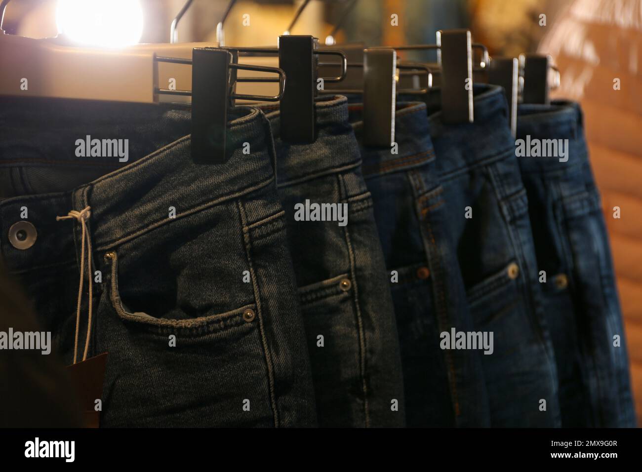 Modern jeans hanging on clothing rack in shop, closeup Stock Photo - Alamy