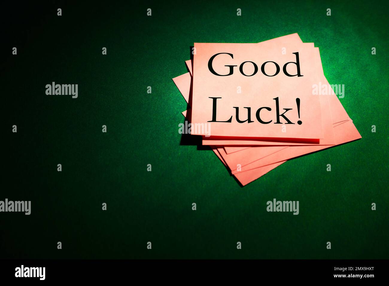 Pink notes with phrase GOOD LUCK on dark green background, above view ...