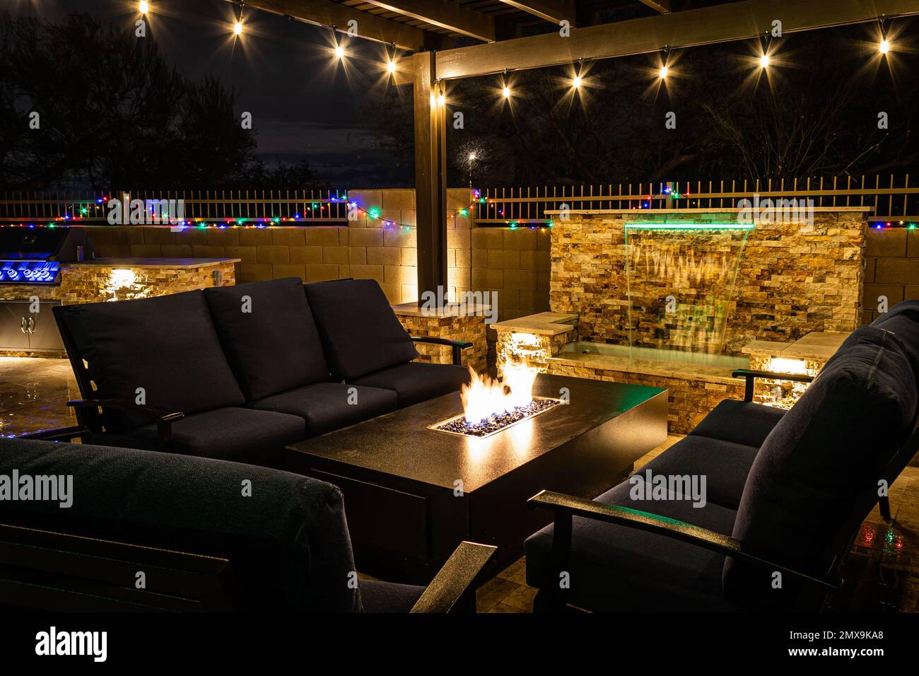 A resort style backyard at night with a waterfall, pergola, and a ...
