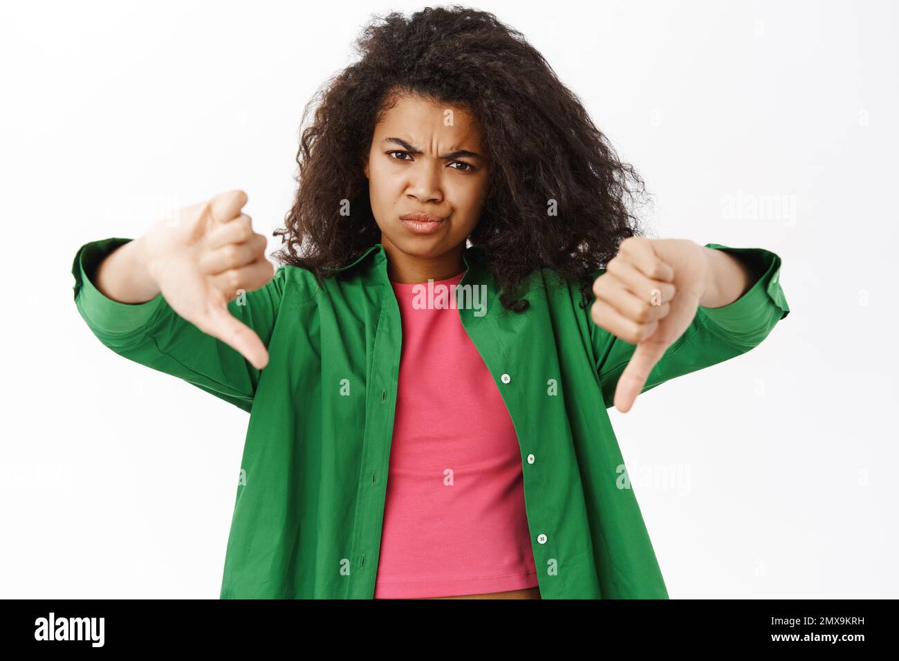 Portrait of disappointed young woman shows thumbs down, dislike ...