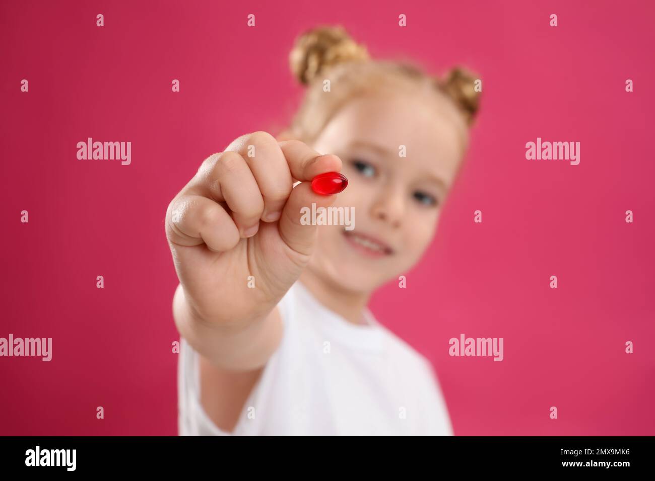Little girl with vitamin pill against pink background, focus on hand ...