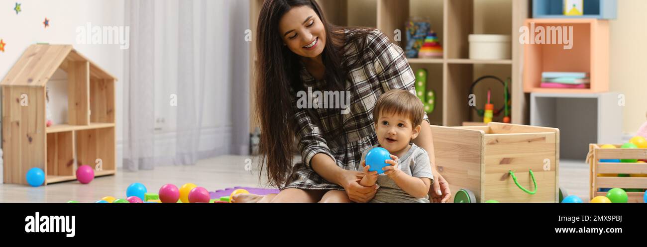 Young nanny and cute little baby playing with toys at home. Banner ...