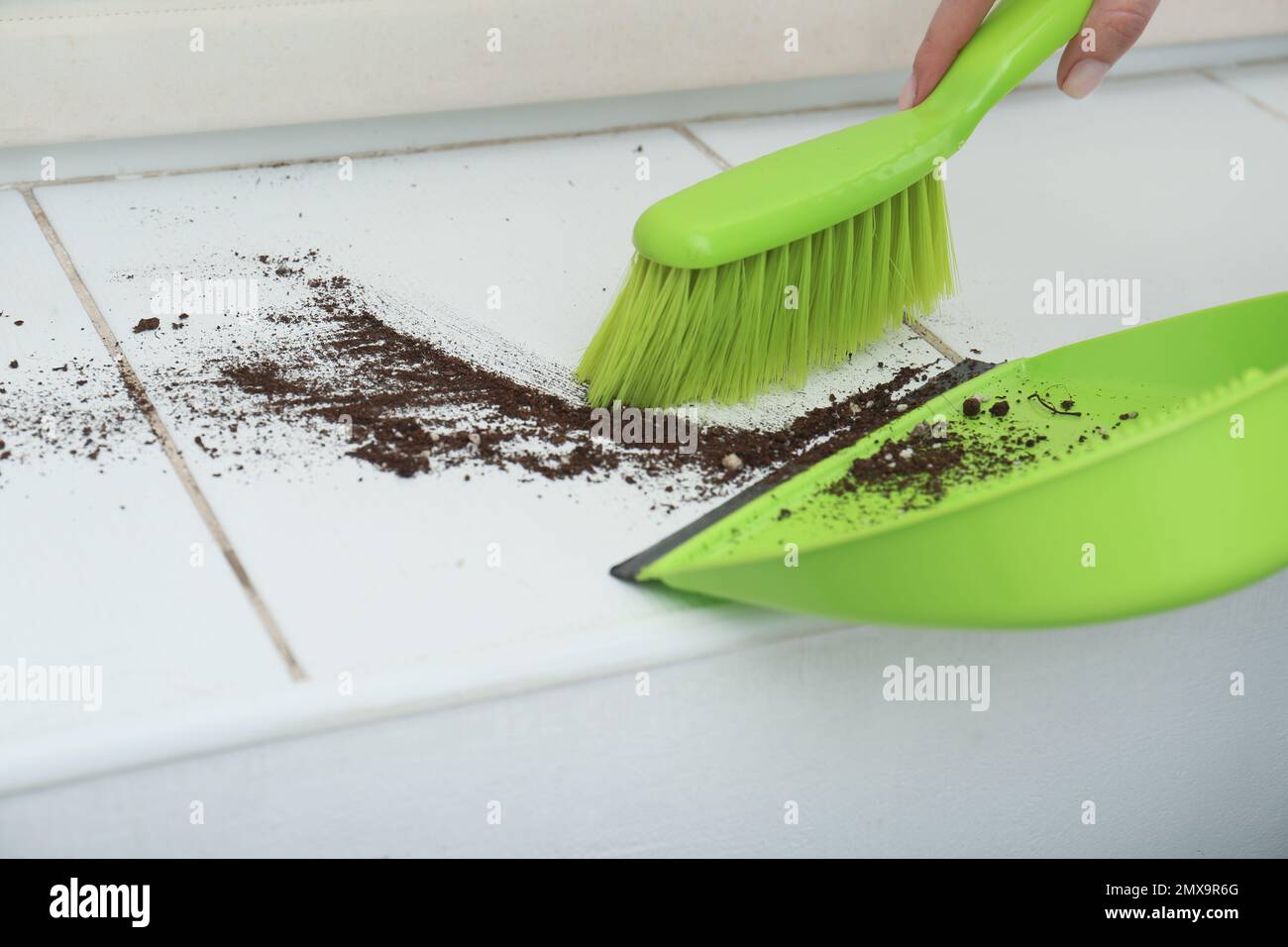 Woman sweeping away scattered soil from window sill with brush, closeup ...
