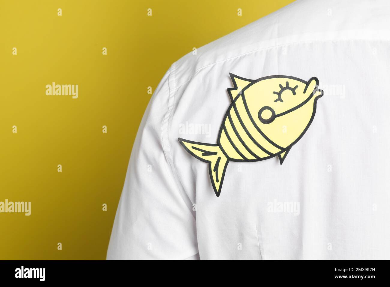 Man with paper fish sticker on back against yellow background, closeup ...