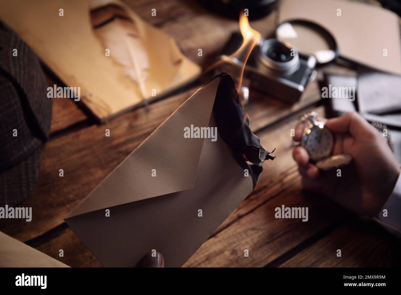 Detective with burning envelope and pocket watch at wooden table ...