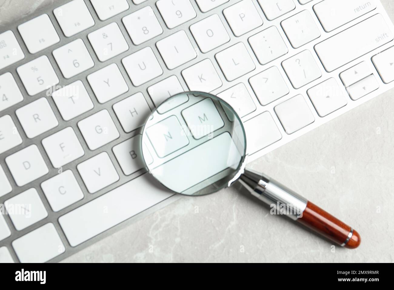 Magnifying glass and computer keyboard on light grey marble table, top ...
