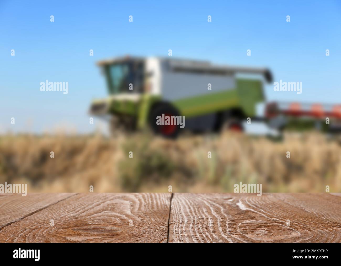 Empty wooden surface and blurred view of modern combine harvester in ...