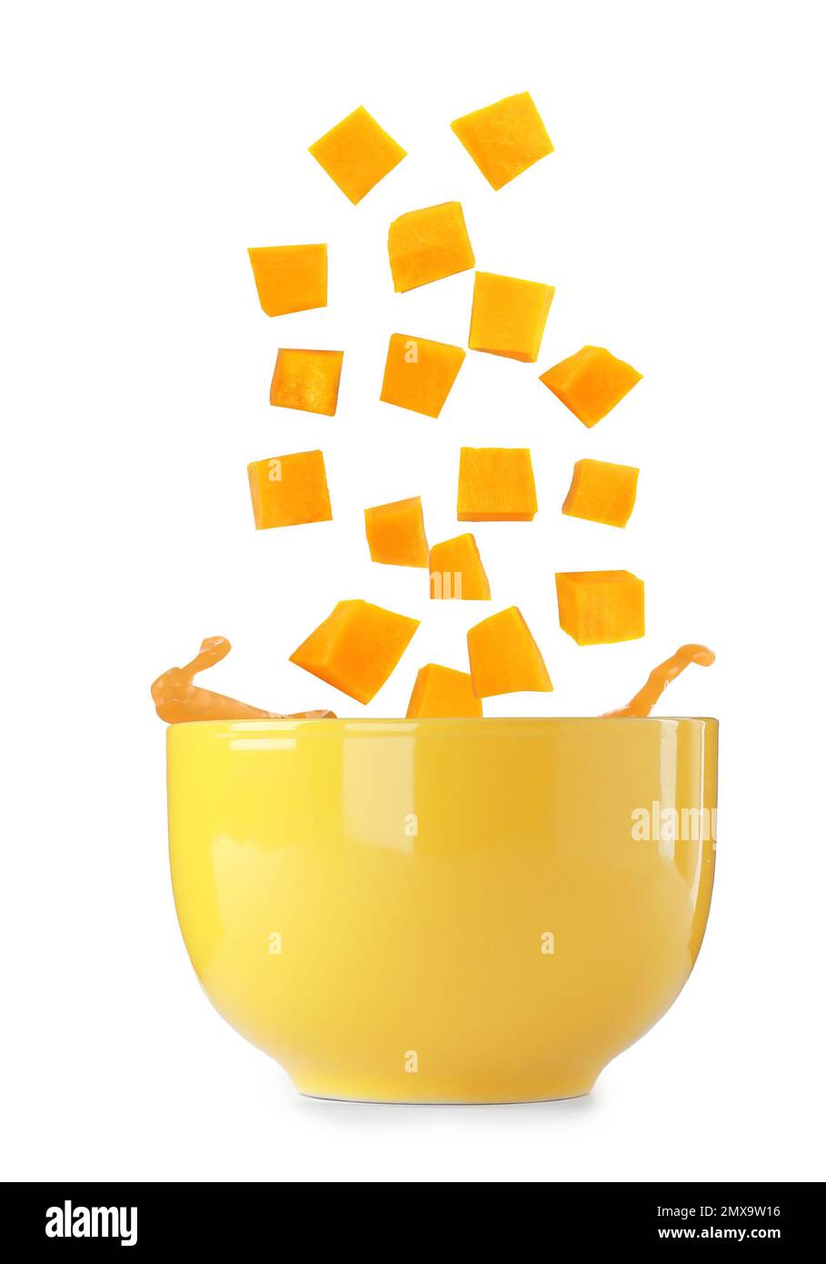 Many pumpkin pieces falling into bowl of homemade soup on white ...