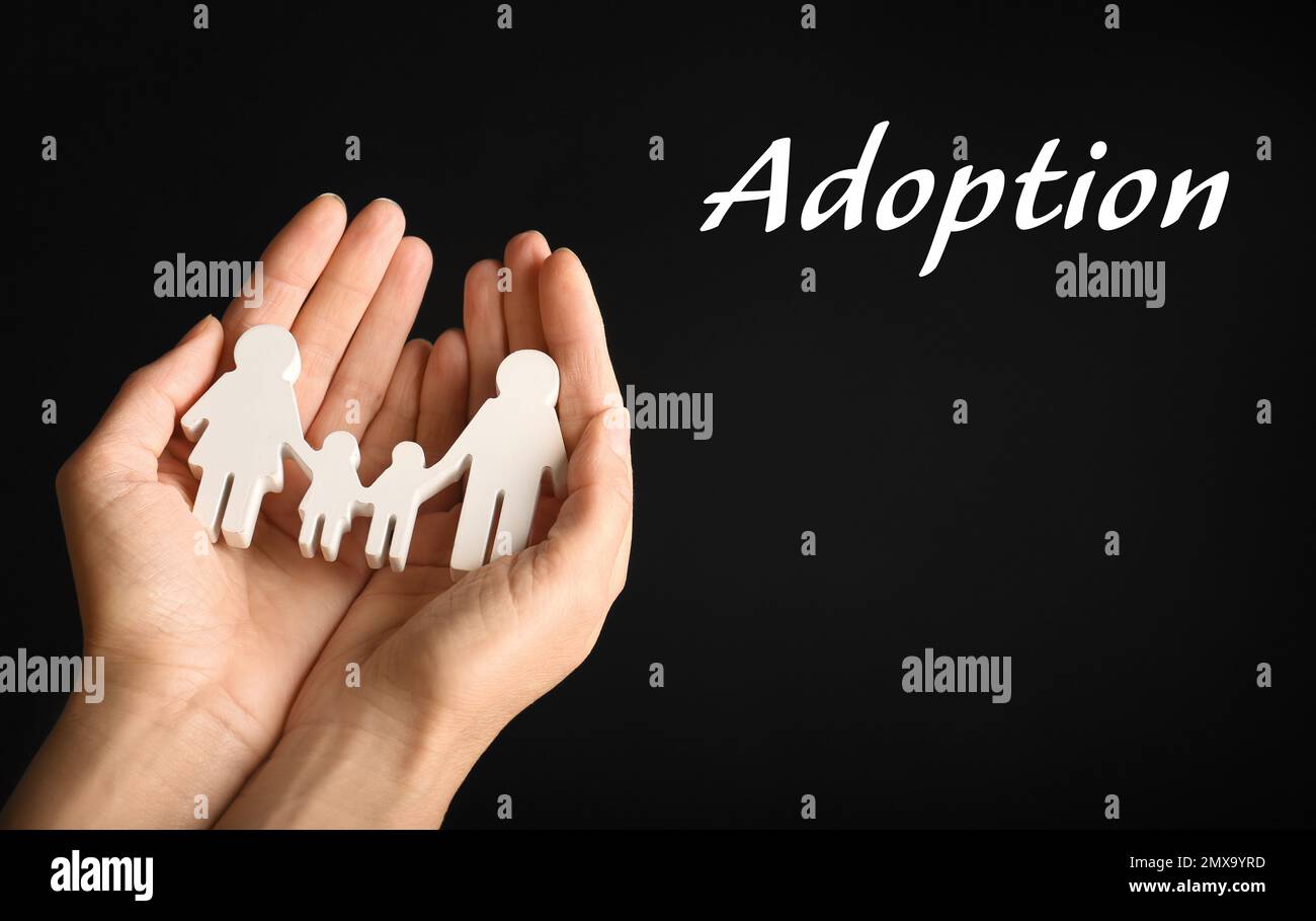 Woman holding figure of family in hands on black background, closeup ...