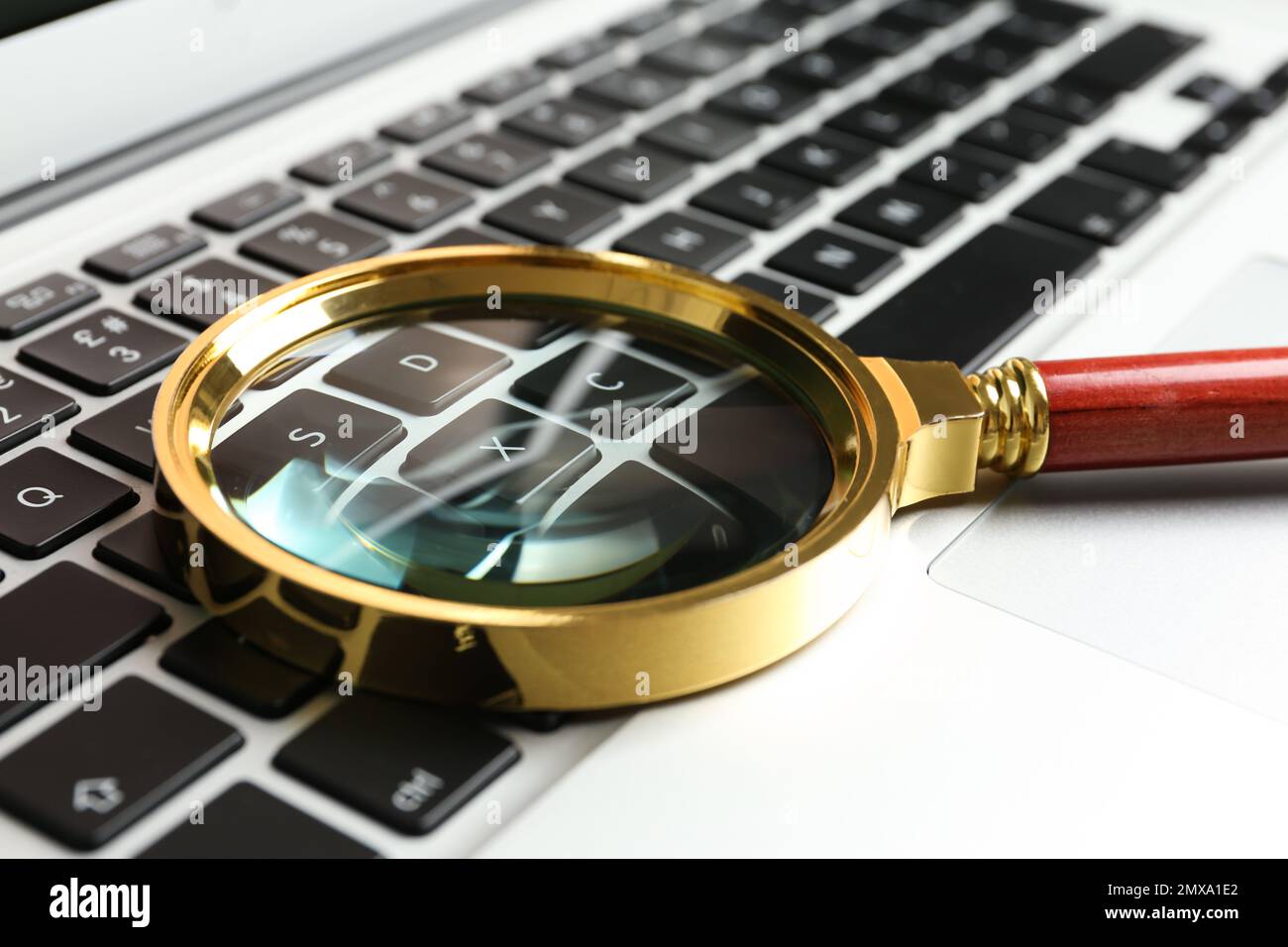 Magnifying glass on keyboard of modern laptop, closeup. Search concept ...