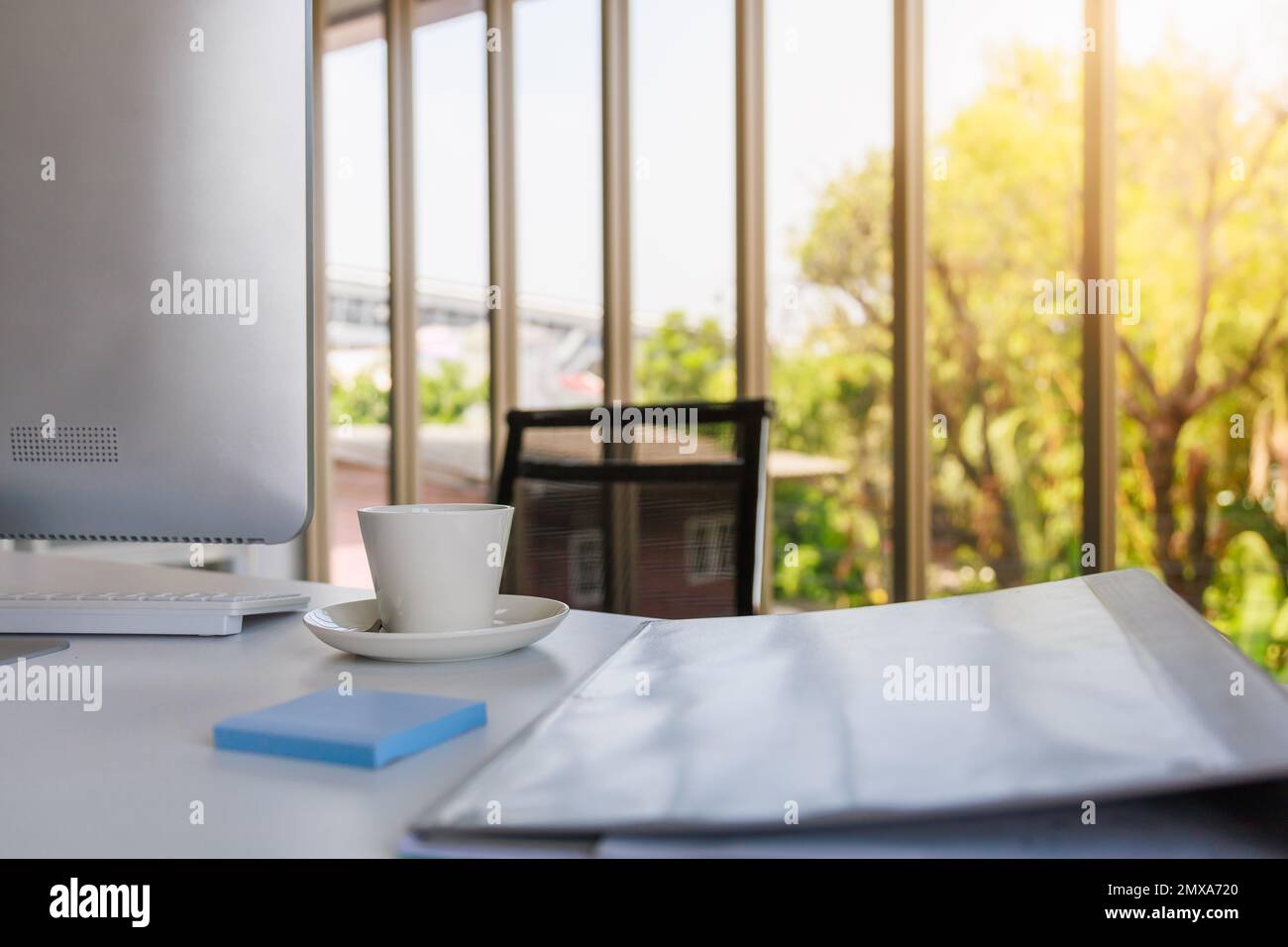 View of office room, closeup of white cup of hot coffee with desktop ...