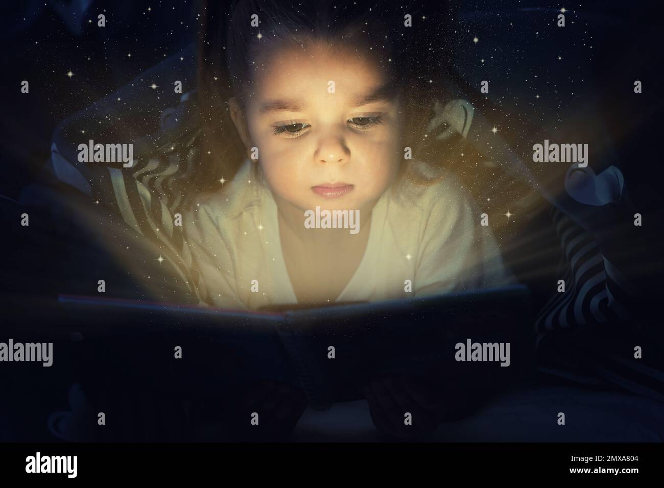 Cute little child reading magic book in darkness Stock Photo - Alamy