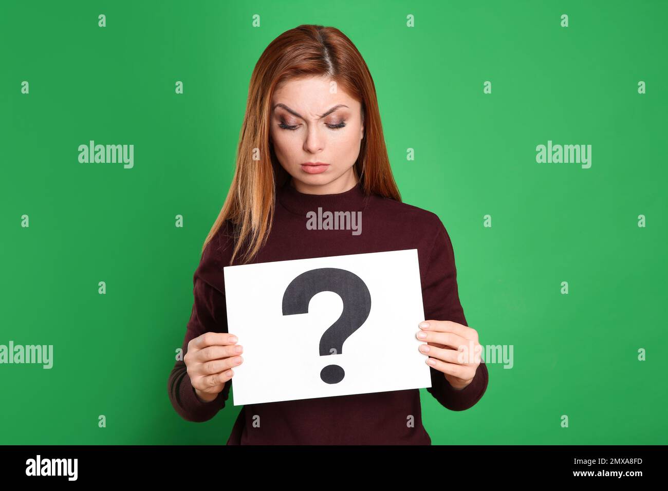 Confused woman holding question mark sign on green background Stock ...