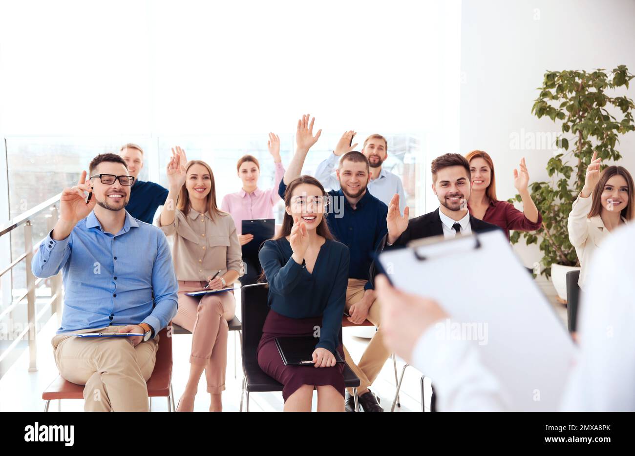 People raising hands to ask questions at business training indoors ...