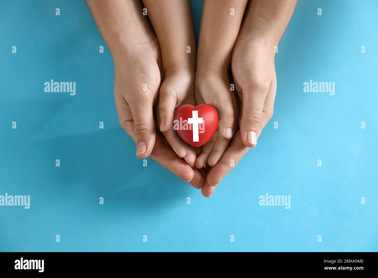 Mother and her child holding heart with cross symbol on light blue ...