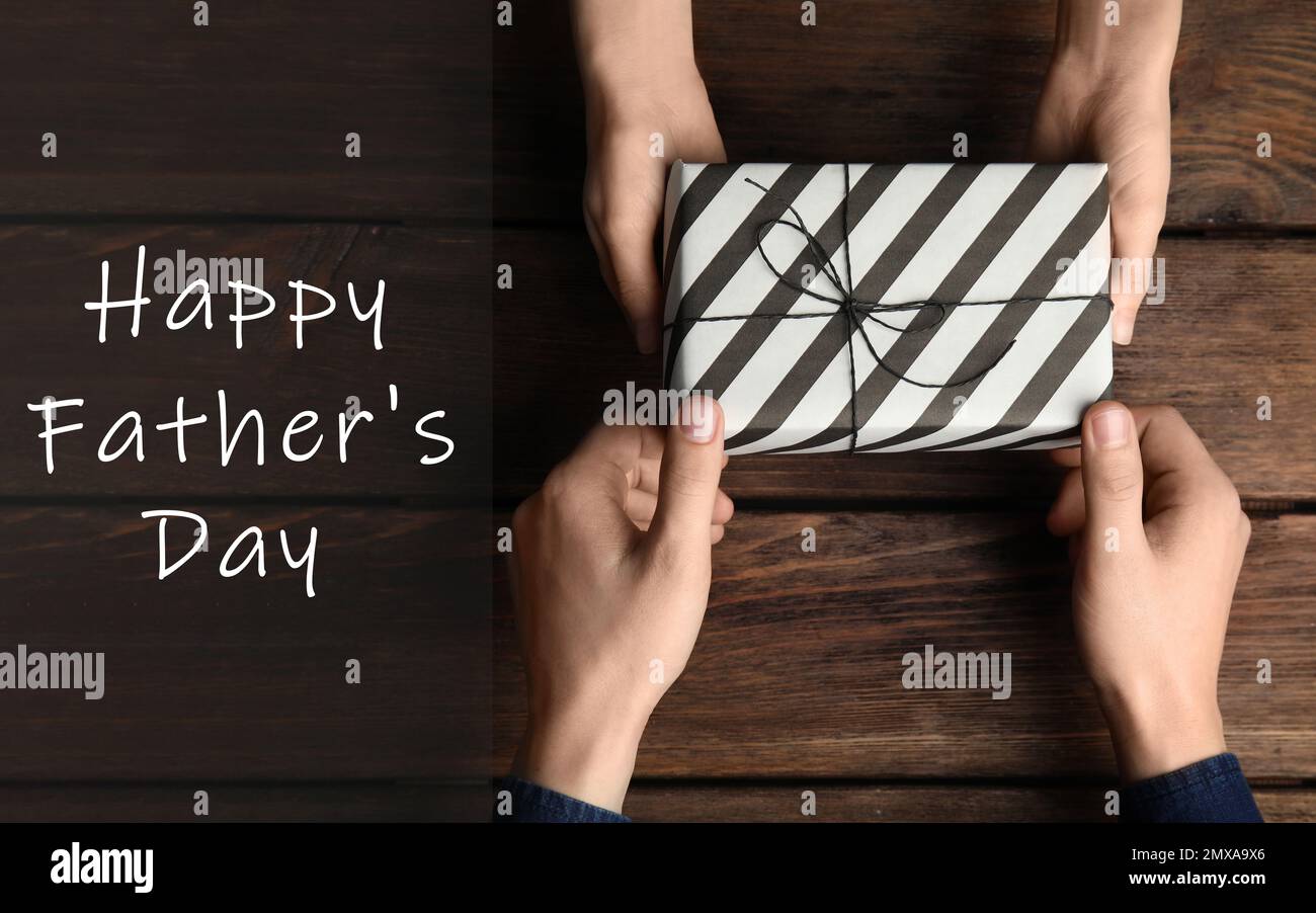 Daughter giving present to her dad over wooden table, top view. Happy ...